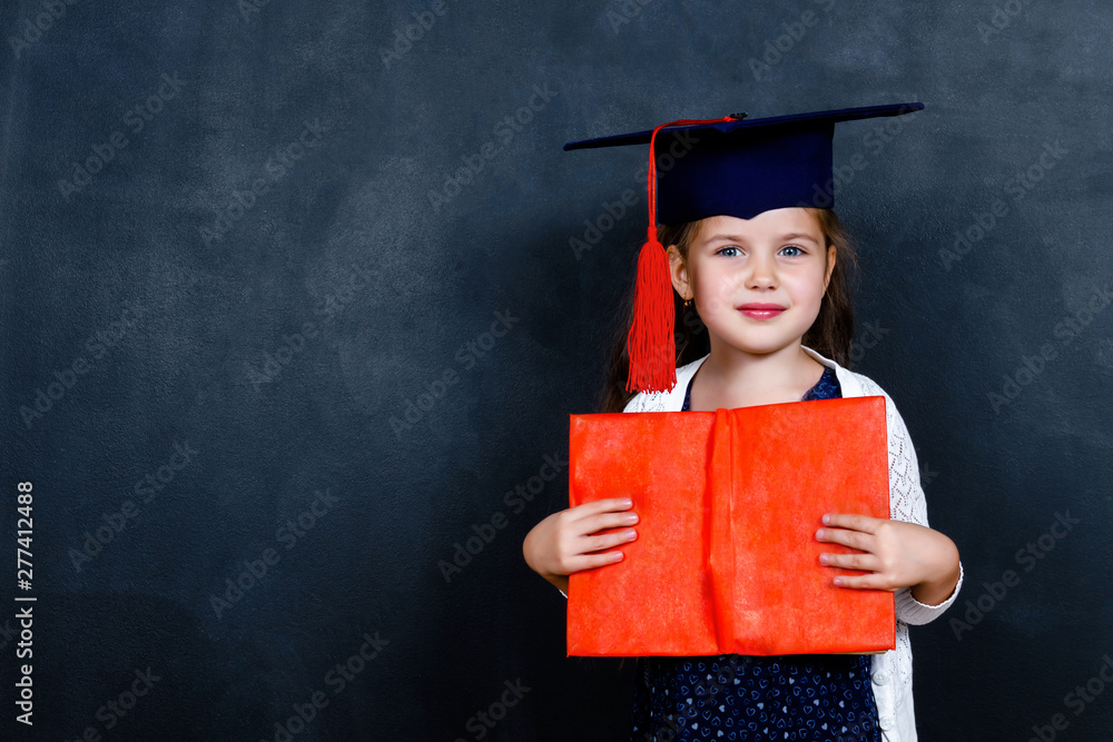 Intelligent smart schoolgirl girl with student bachelor hat reading ...