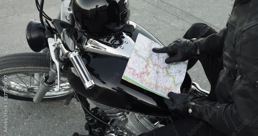 Man motorcyclist chooses the route on map sitting on his bike, hands ...