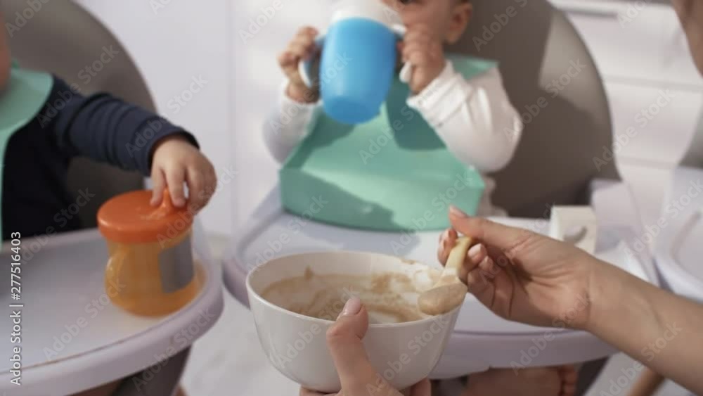 Over-shoulder shot of mother mixing baby food in bowl and feeding her 1 ...