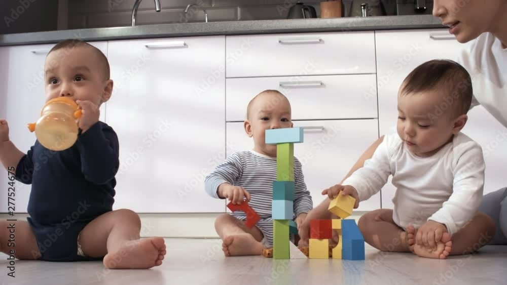 Full shot of 1-year-old mixed race identical triplets sitting on floor ...