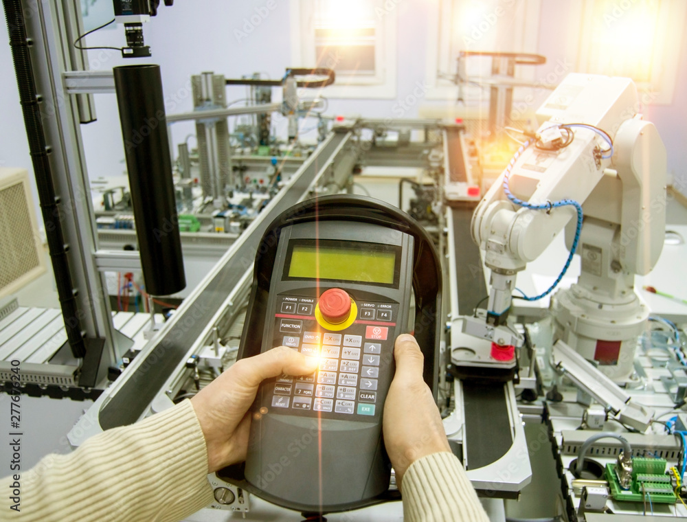 Man is holding teach panel (tablet) to control a robotic arm which is integrated on smart ...