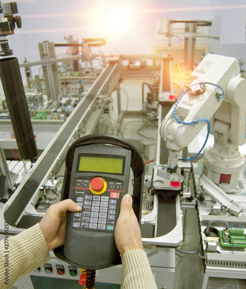 Man is holding teach panel (tablet) to control a robotic arm which is integrated on smart ...