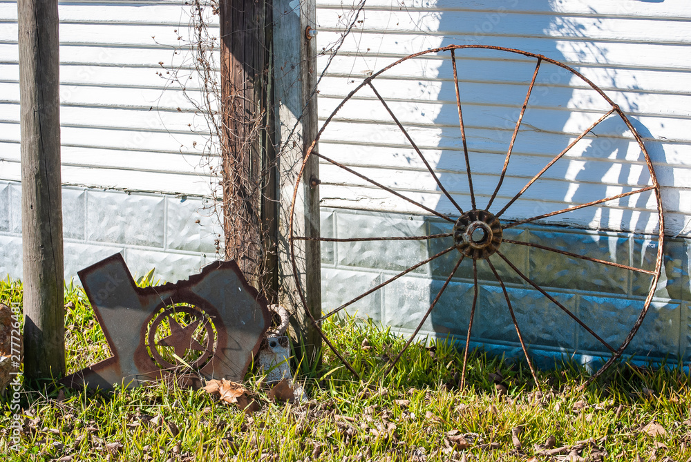rusted wagon wheel spoke texas sign against white wood country building ...