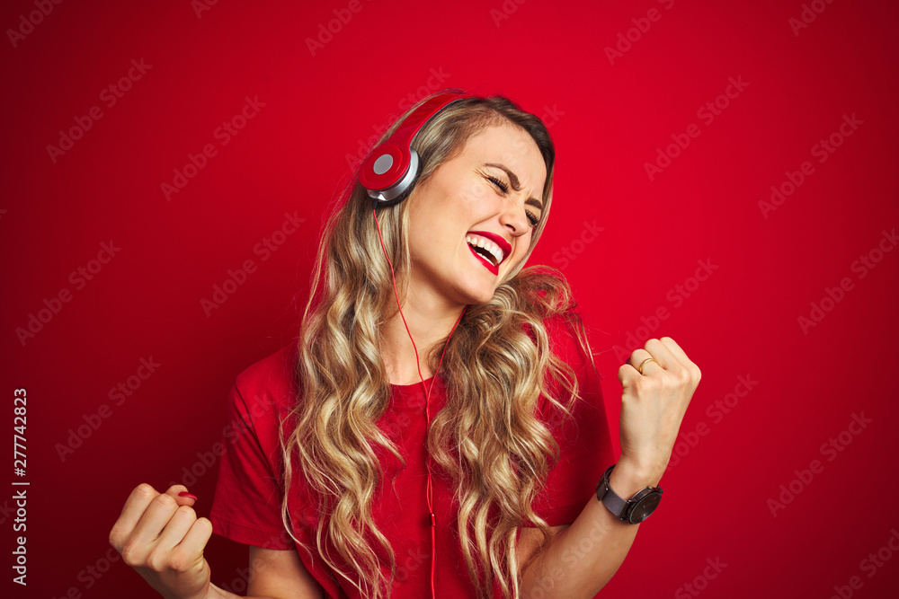 Young beautiful woman wearing headphones over red isolated background ...