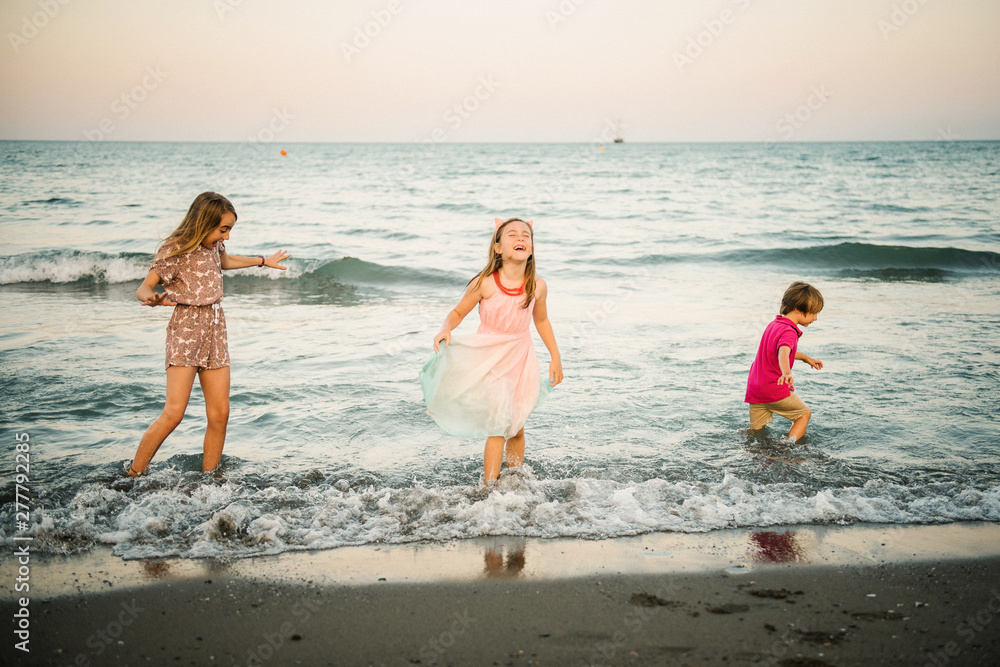 Group of little boy with two sisters playing in shallow wave of water ...