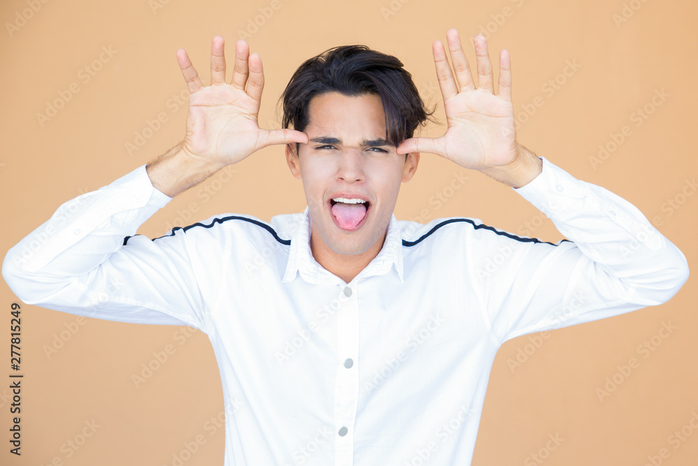 Grimacing guy sticking tongue out and holding hands near temples ...