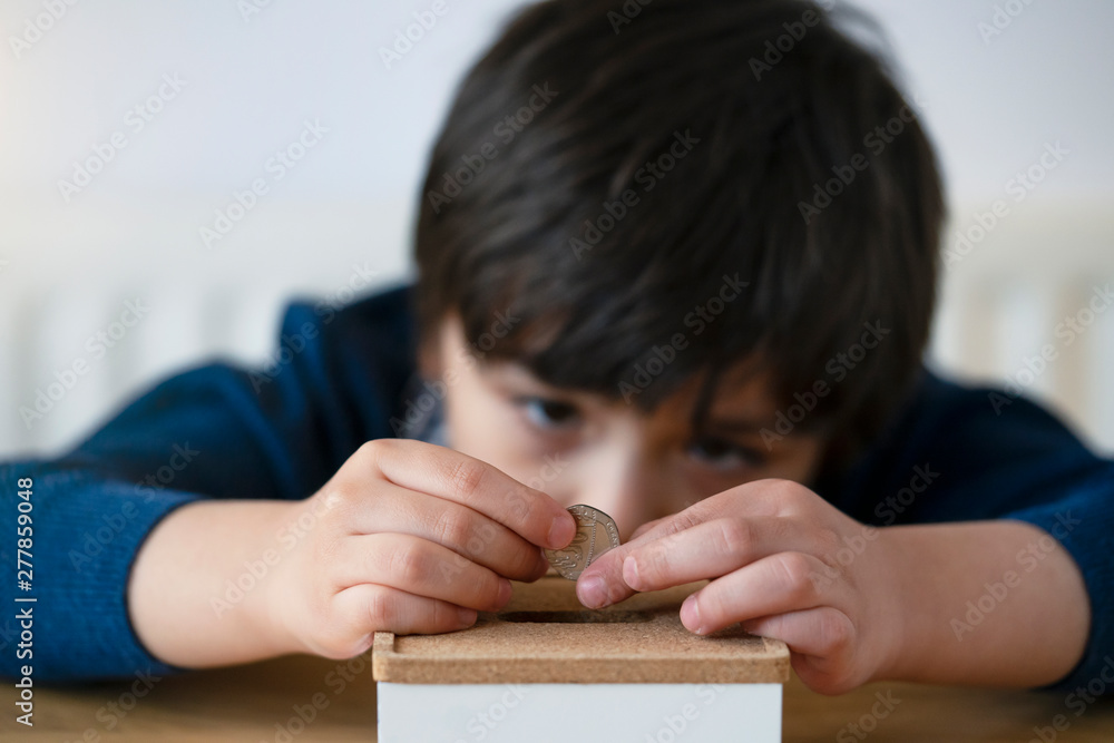Blurry face of kid with thinking face putting 10 pence on money box ...