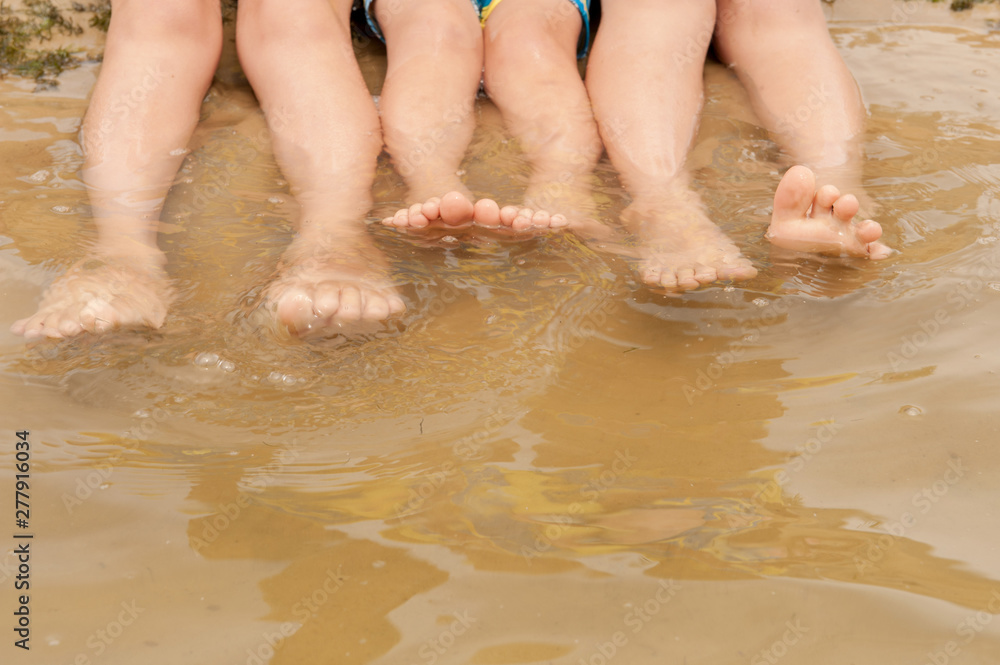 Funny kids in bathing suits sit together on sand with their legs in ...