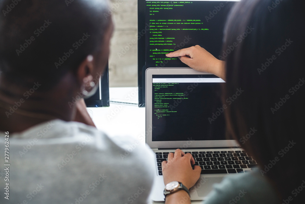 Rear view of female entrepreneur pointing at codes on computer monitor ...