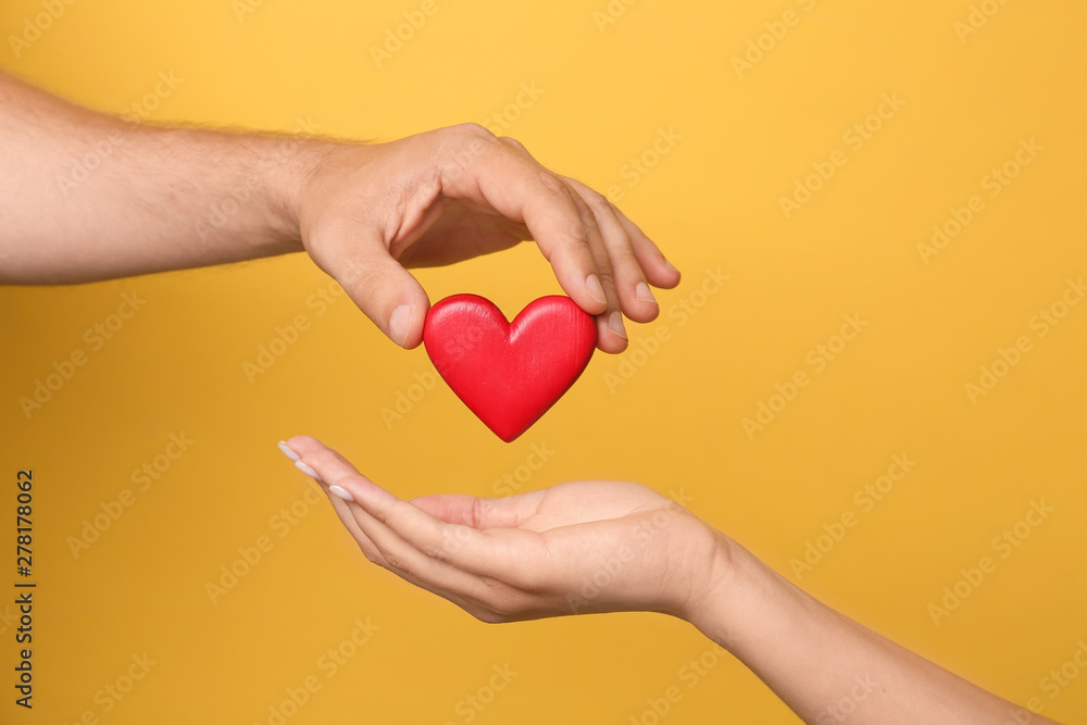 Man giving red heart to woman on yellow background, closeup. Donation ...