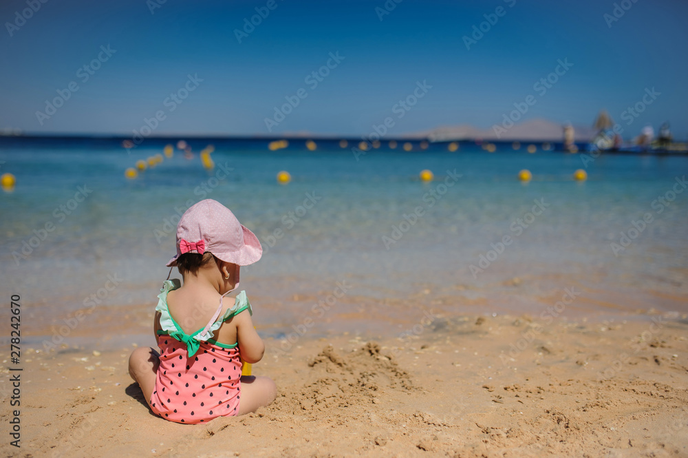 back view photo of a little girl in swimsuit and pink hat sitting on ...