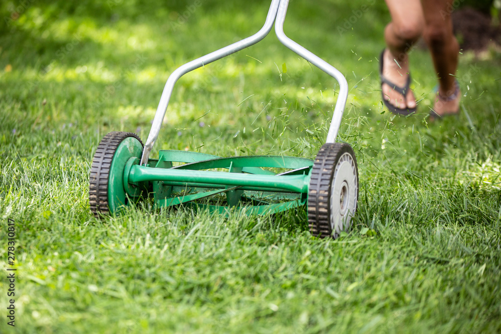Closeup of the head of a push mower as a young girl pushes it forward ...