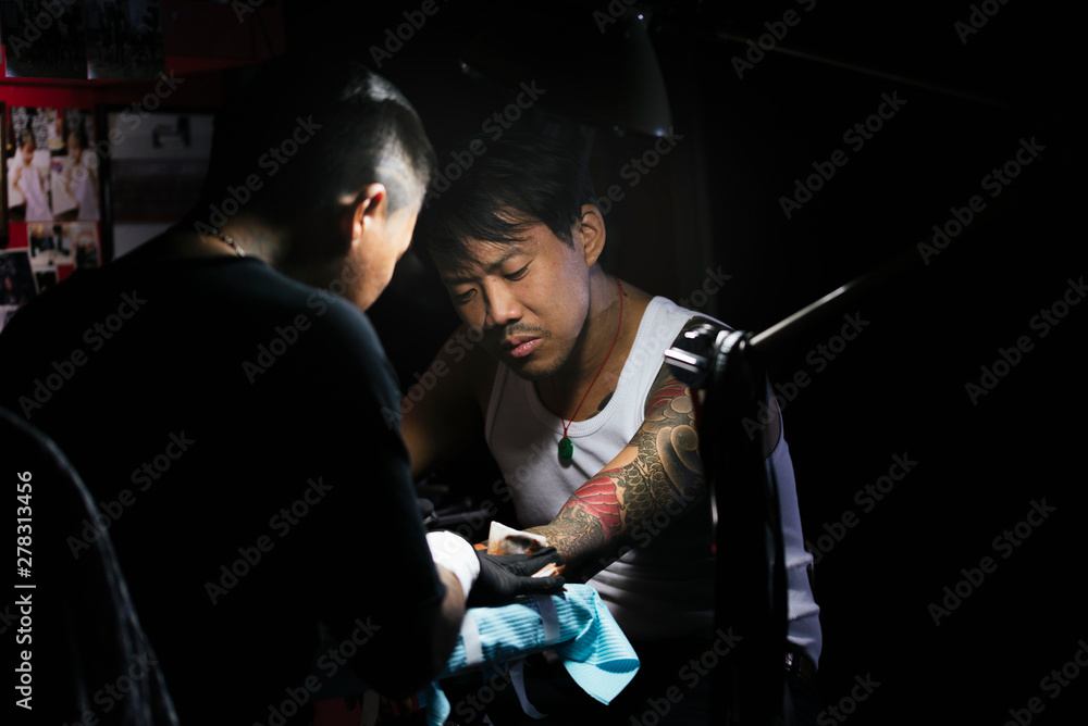 Professional asian tattooer makes a tattoo Stock Photo | Adobe Stock