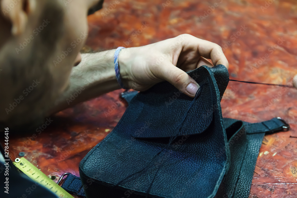 Craftsman intently works with leather. Tanner sews leather goods ...