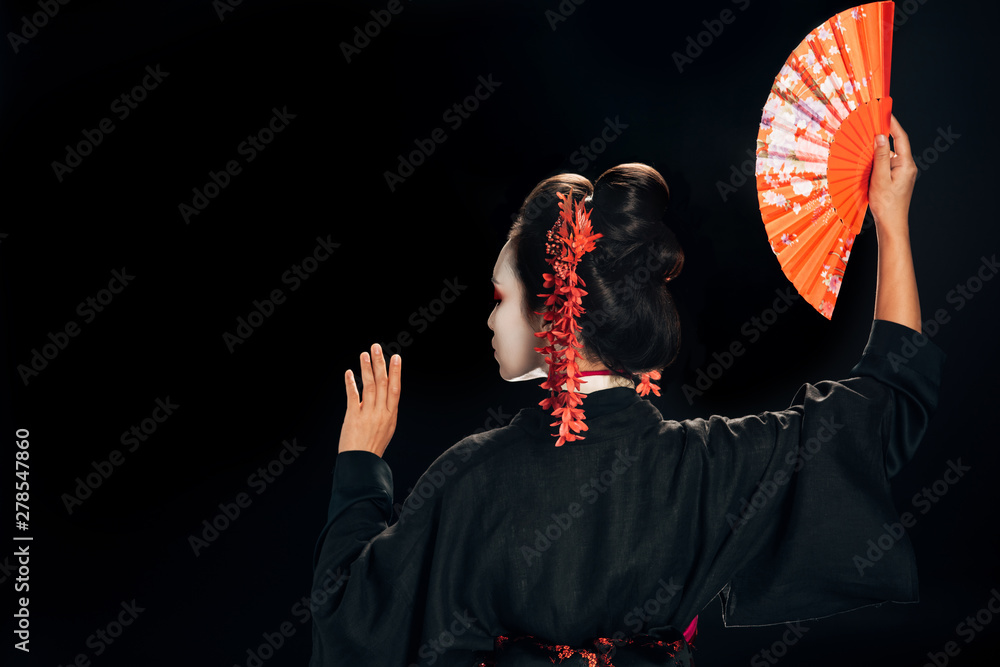 back view of beautiful geisha in black kimono with red flowers in hair ...