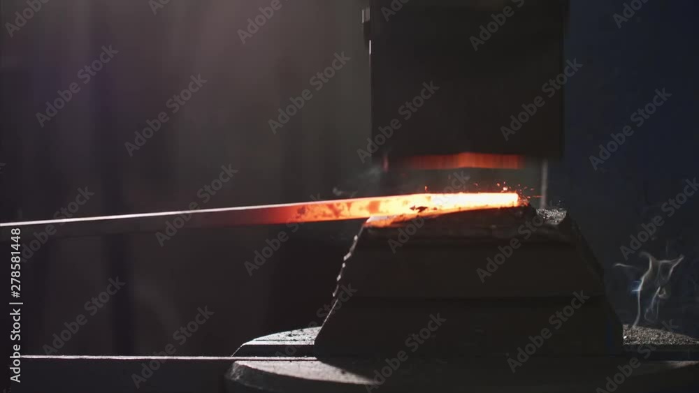 Using hammer machine for shaping hot red metal bar in forge workshop ...