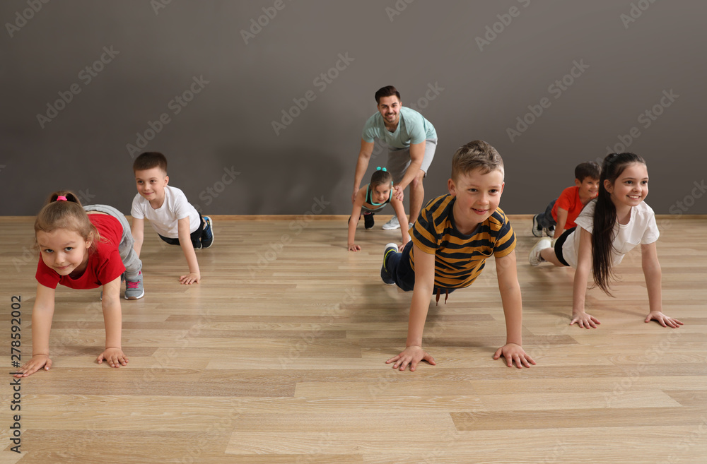 Cute little children and trainer doing physical exercise in school gym ...