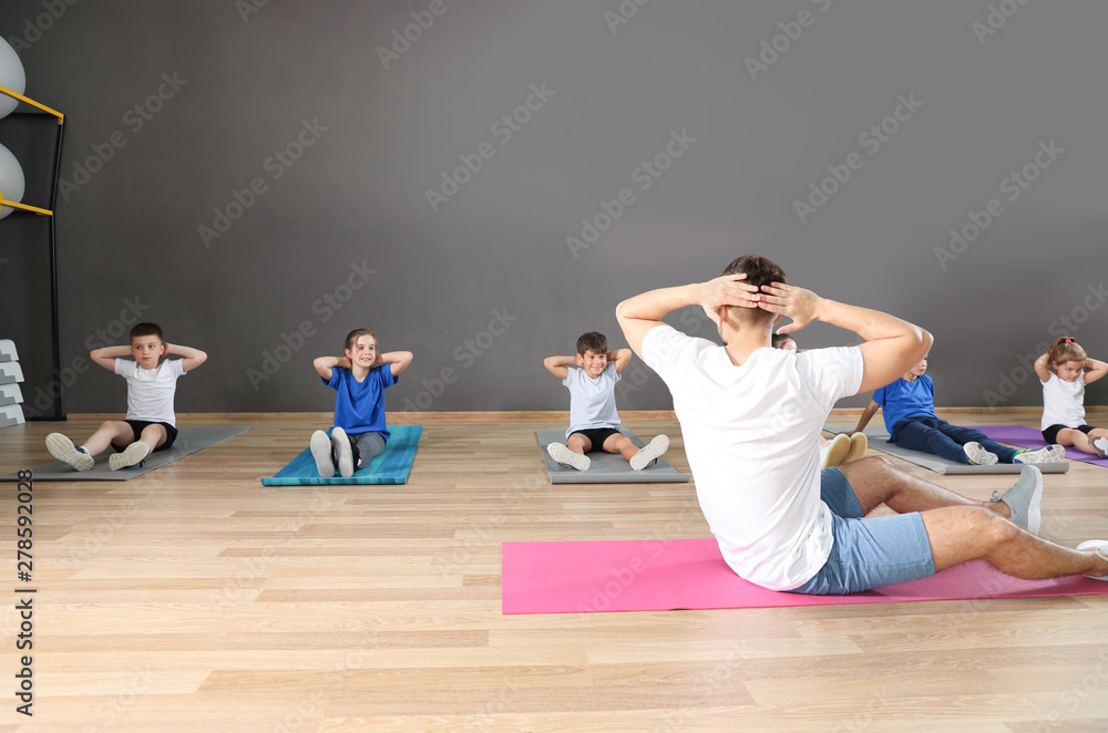 Cute little children and trainer doing physical exercise in school gym ...