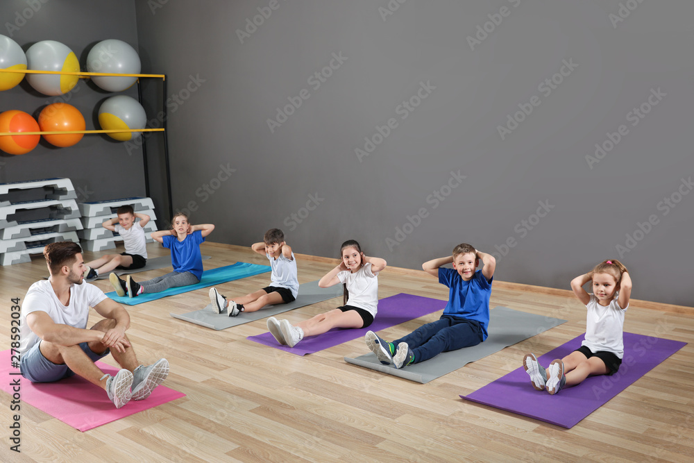 Cute little children and trainer doing physical exercise in school gym ...
