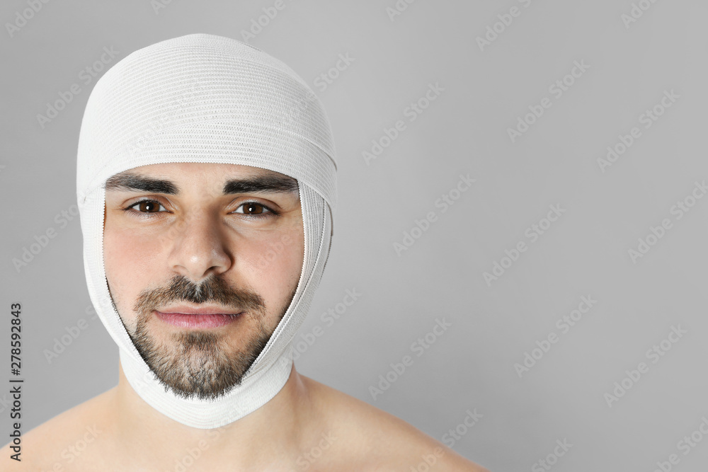 Bandaged young man after plastic surgery operation on grey background ...