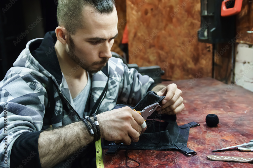 Craftsman intently works with leather. Tanner sews leather goods ...