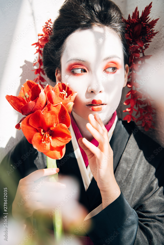 selective focus of sakura branches and beautiful geisha holding red ...