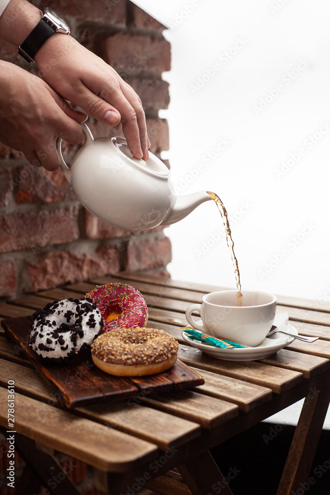 Woman is pouring tea for a tea party with doughnuts: strawberry, oreo ...