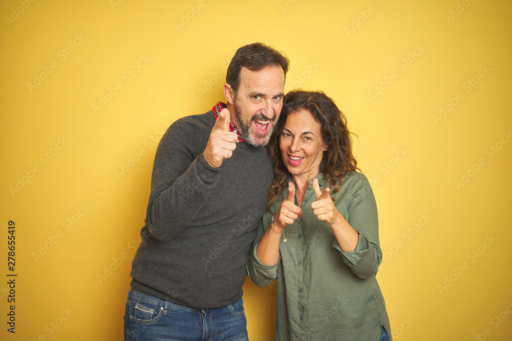 Beautiful middle age couple over isolated yellow background pointing ...