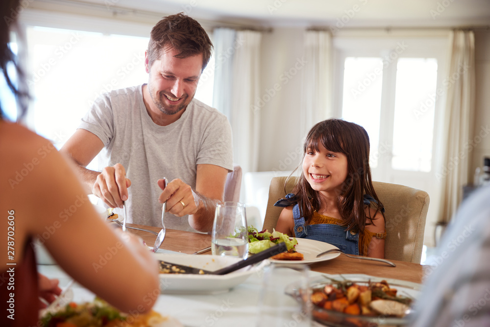 Young girl waiting for her dad to serve food at the dinner table during ...