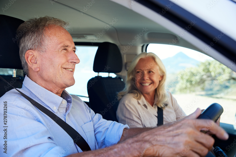 Senior white man driving car, his wife beside him in the front ...