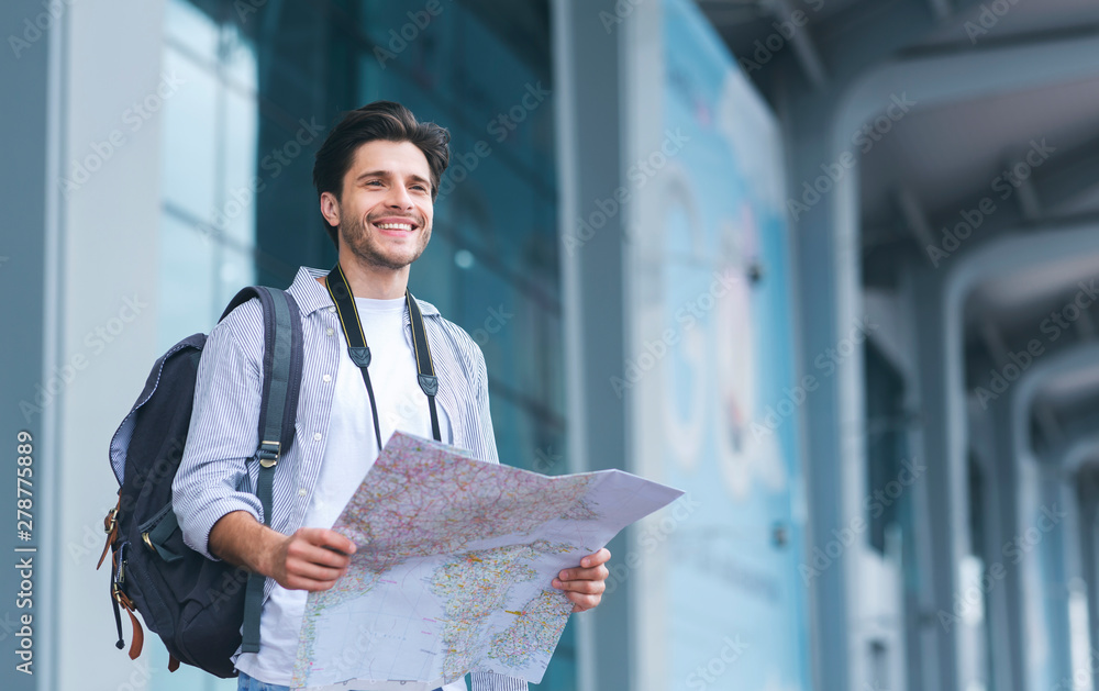Cheerful man traveler holding map, studying new destinations at airport ...