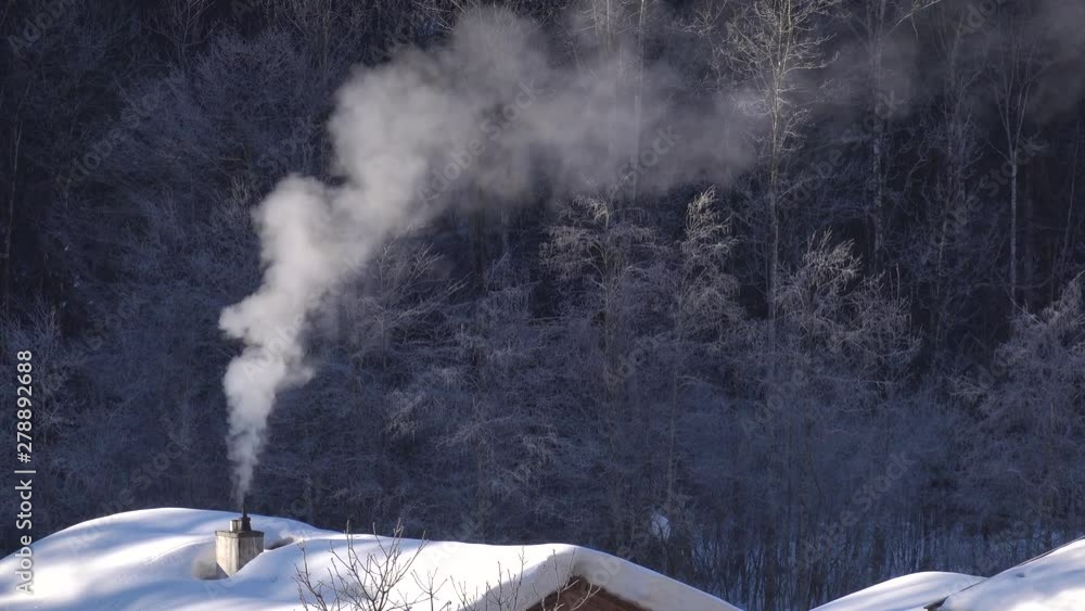 Smoke coming out of a chimney on the roof of a house in winter with ...