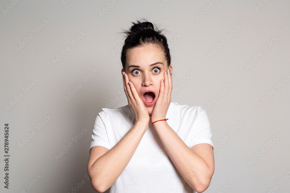Astonished, shocked woman emotionally holds hands on her face, opened ...