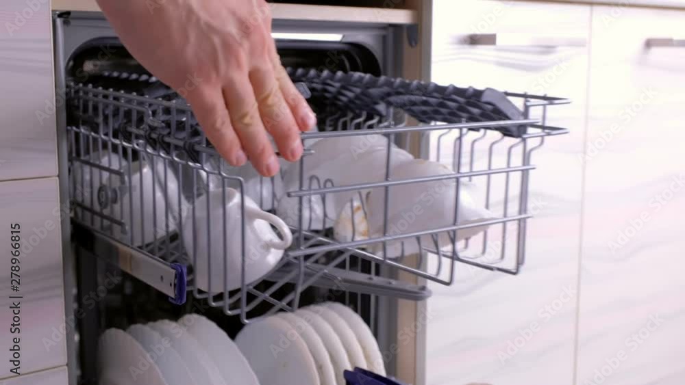 Man's hand is putting white cup and glass and closing dishwasher with ...