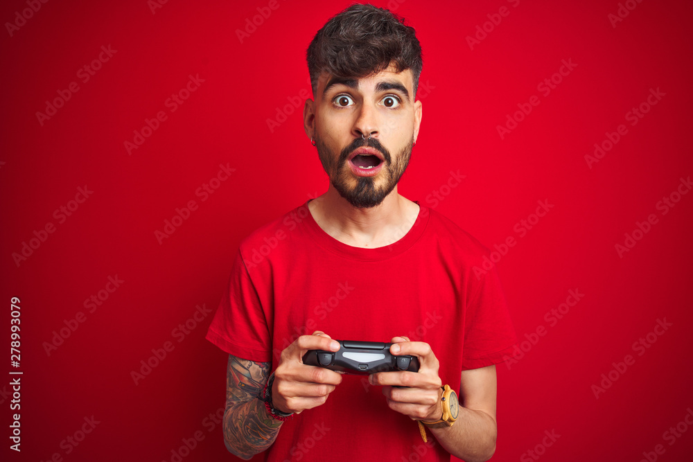 Young gamer man with tattoo playing video game standing over isolated ...