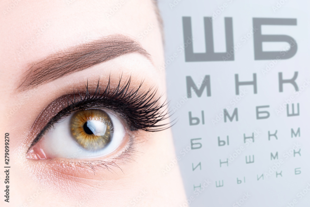 Female eye on the blurry russian eye chart background close up. Visual ...