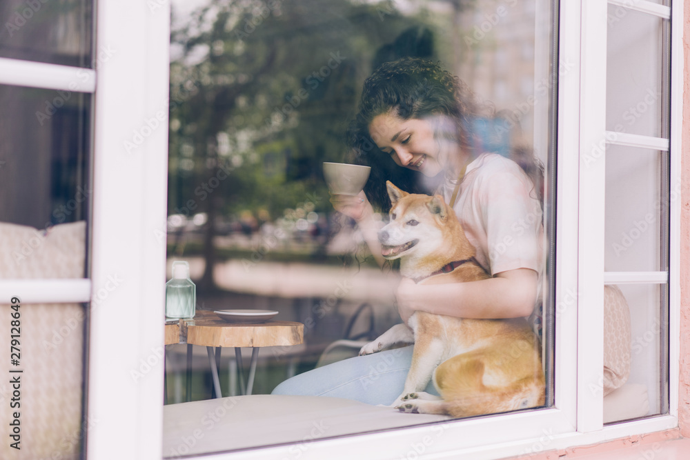 Beautiful young woman is drinking tea in cafe and hugging cute shiba ...