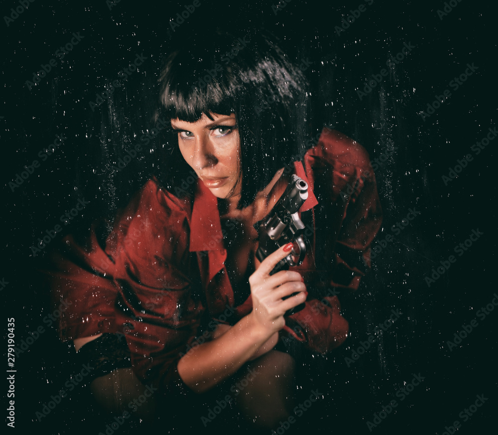 Beautiful woman with a revolver in her hands and raindrops flowing down ...