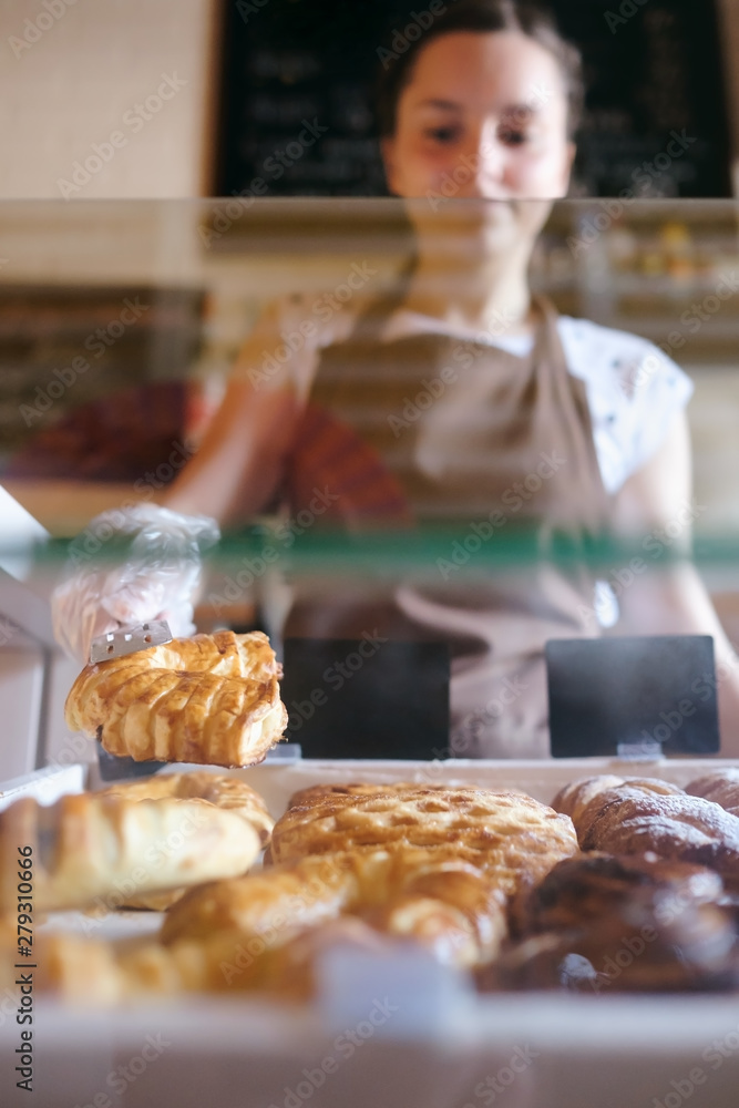 Pretty smiling female worker selecting muffins from a counter display ...