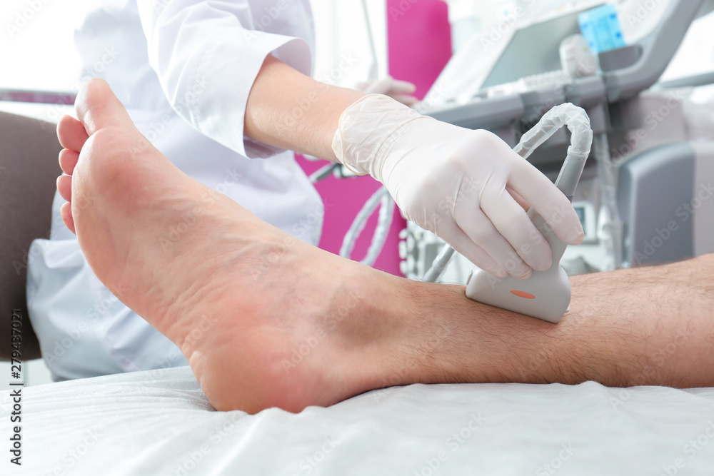 Doctor conducting ultrasound examination of patient's leg in clinic ...