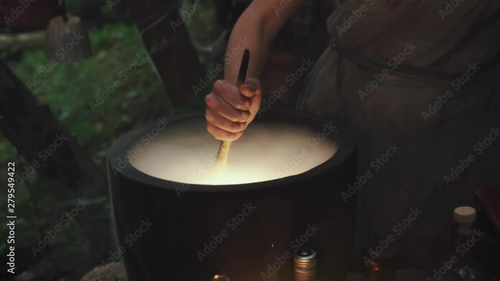 human hand of old woman evil witch is stirring potion in bubbling vat ...