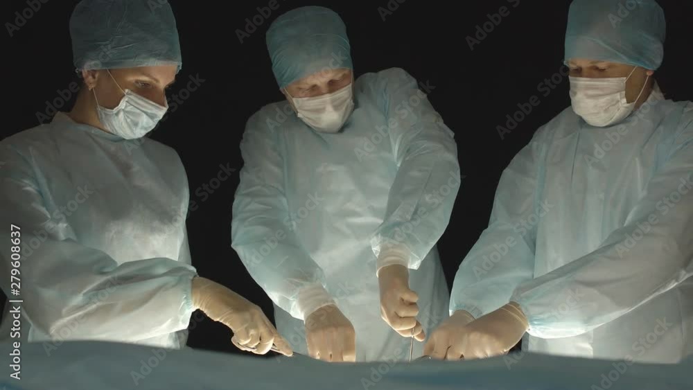 Three surgeons, a man and a woman, perform surgery in the operating ...