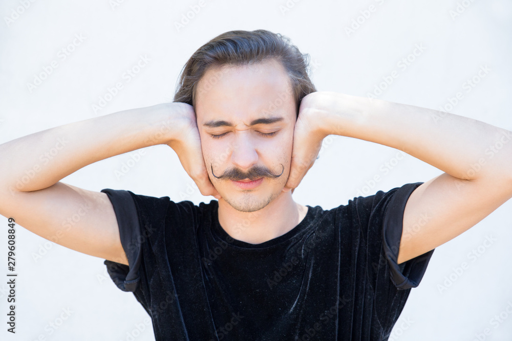 Deaf young man with closed eyes covering ears. Handsome guy cannot hear ...