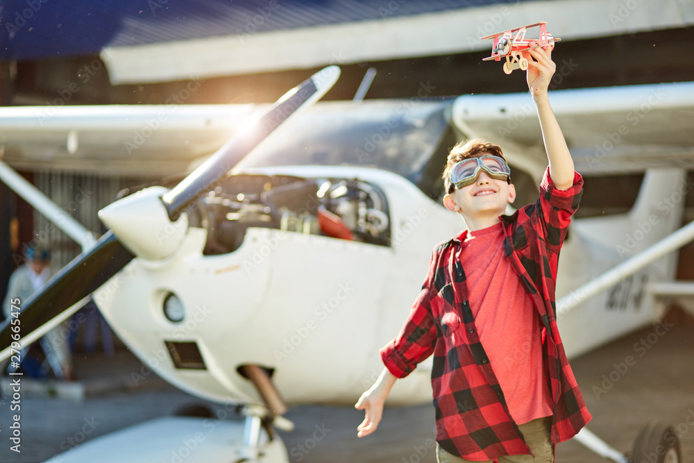 happy little boy playing with small toy airplane near hangar and white ...