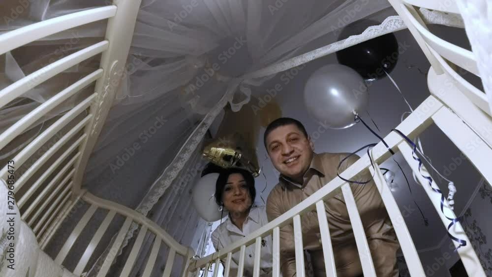 Family concept. Mom and dad are looking at their baby in cot. Baloons ...