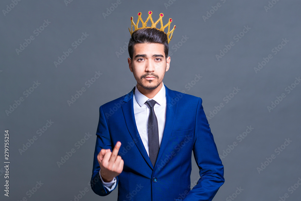 A young man in a suit with a crown on his head shows the middle finger ...