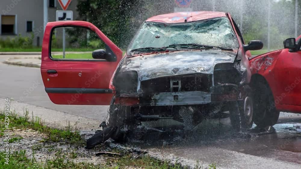 A jet of water is extinguishing a burning vehicle. Firefighters are ...