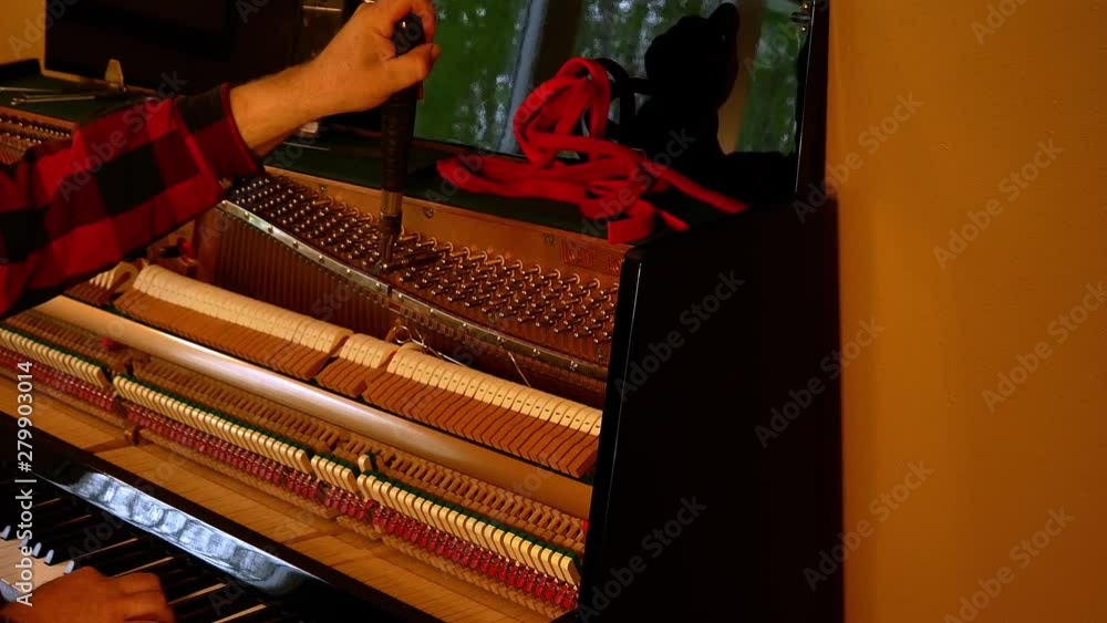 Technician tuning an upright piano by playing black and white keys and ...
