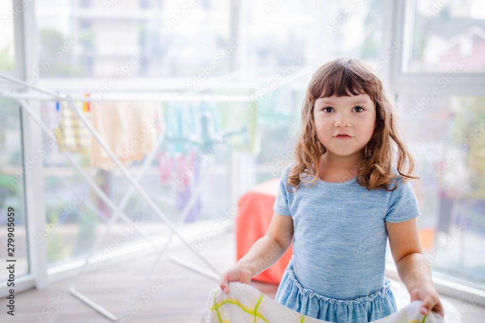 Child in laundry room. Clean washed clothes on drying rack. Mother's ...