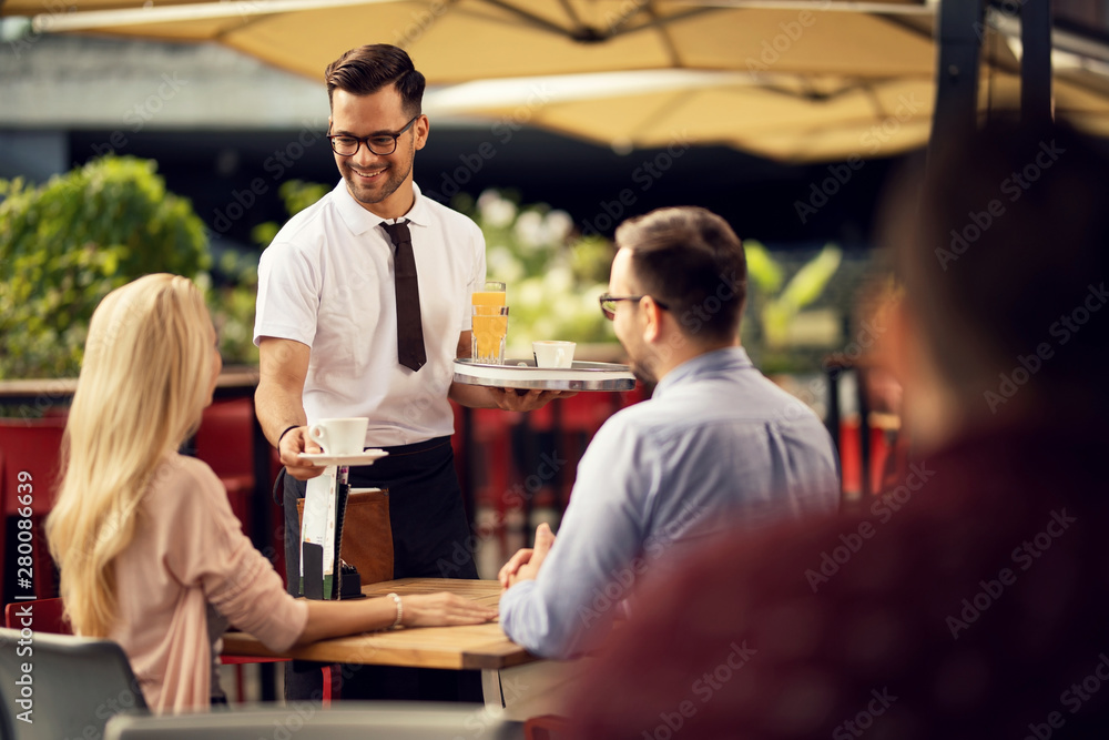 Young smiling waiter serving coffee to guests in a cafe. Stock Photo ...